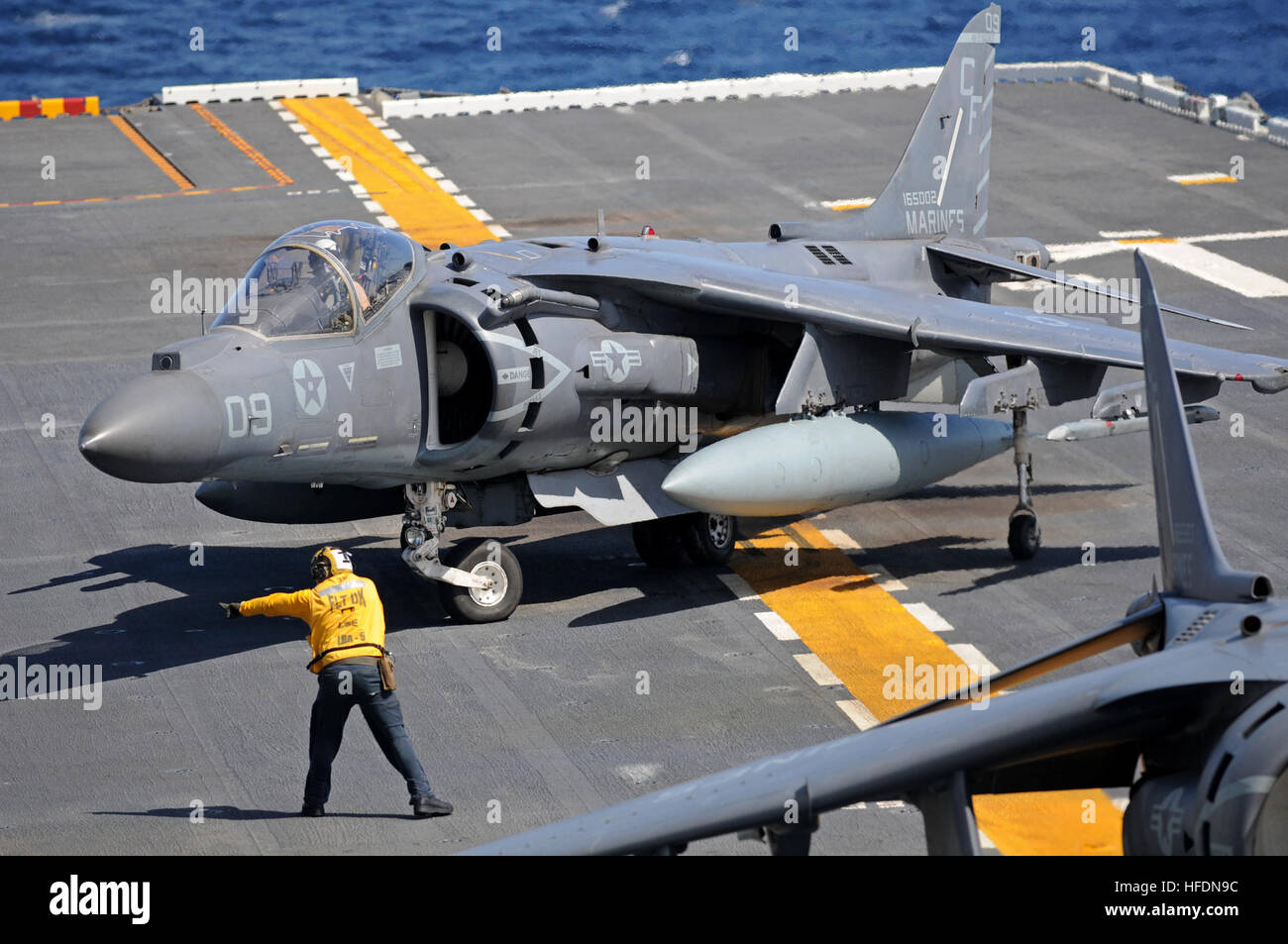 A Sailor directs an AV-8B Harrier from VMA-211 during flight operations ...