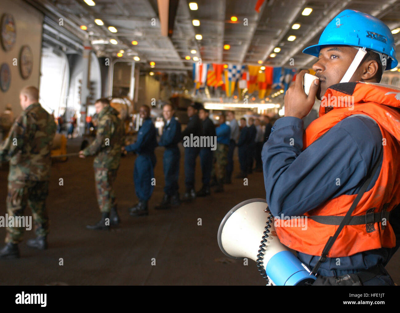 A seaman directs a line-handling team with a bullhorn in the hangar bay ...