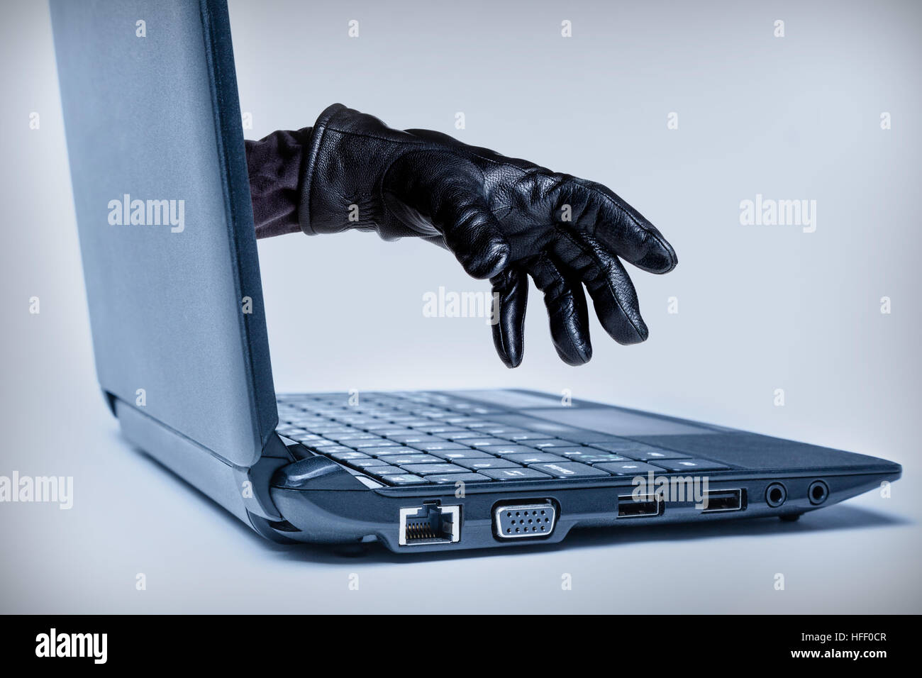 A gloved hand reaching out through a laptop, signifying a cybercrime or ...