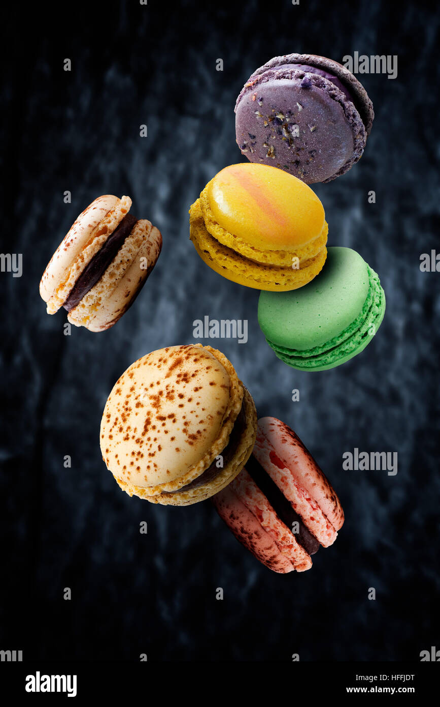 Assorted multi flavored macaroons floating against dark background ...