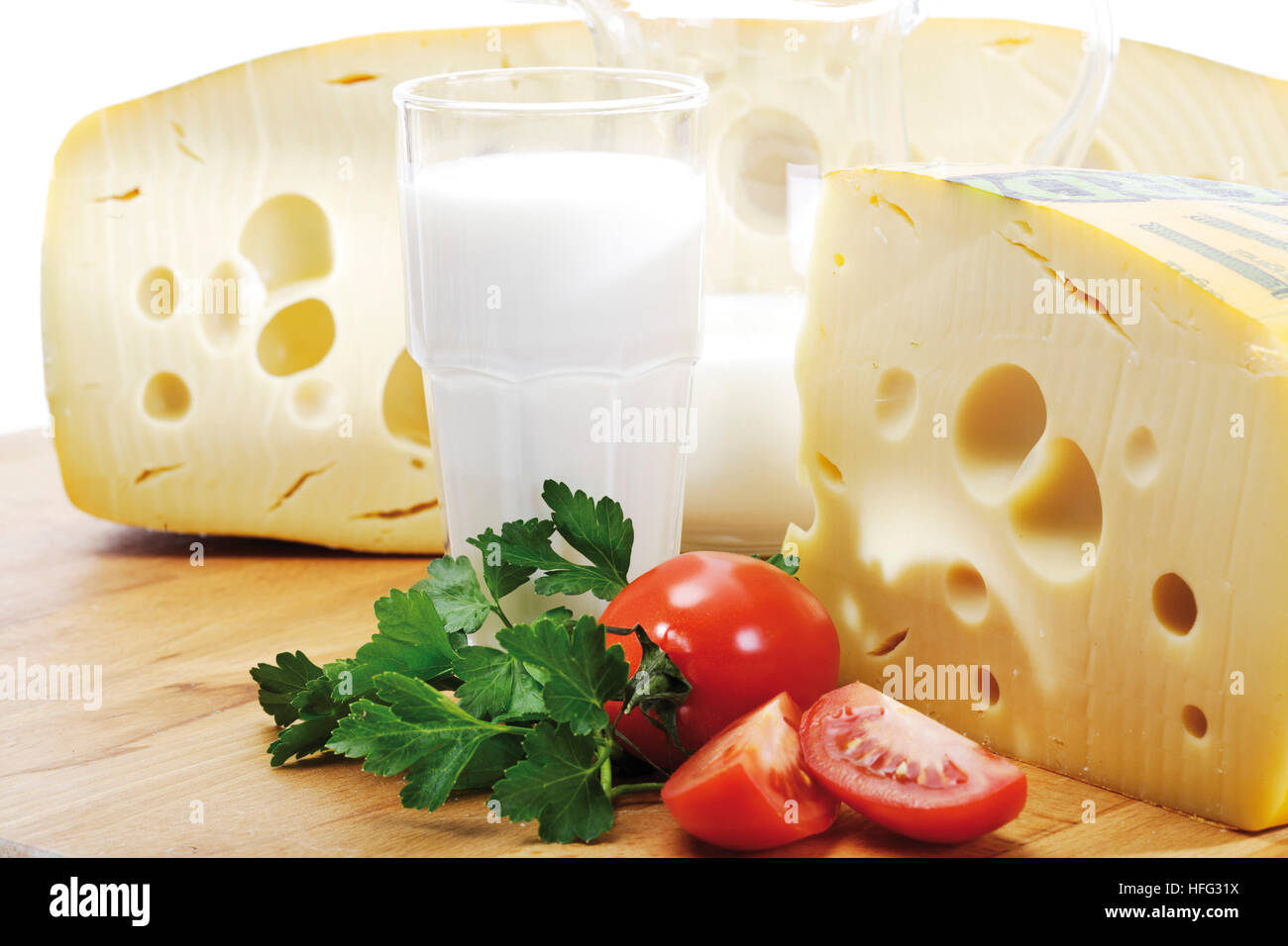 Whole and quarter cheese wheel, a glass of milk and tomatoes Stock ...