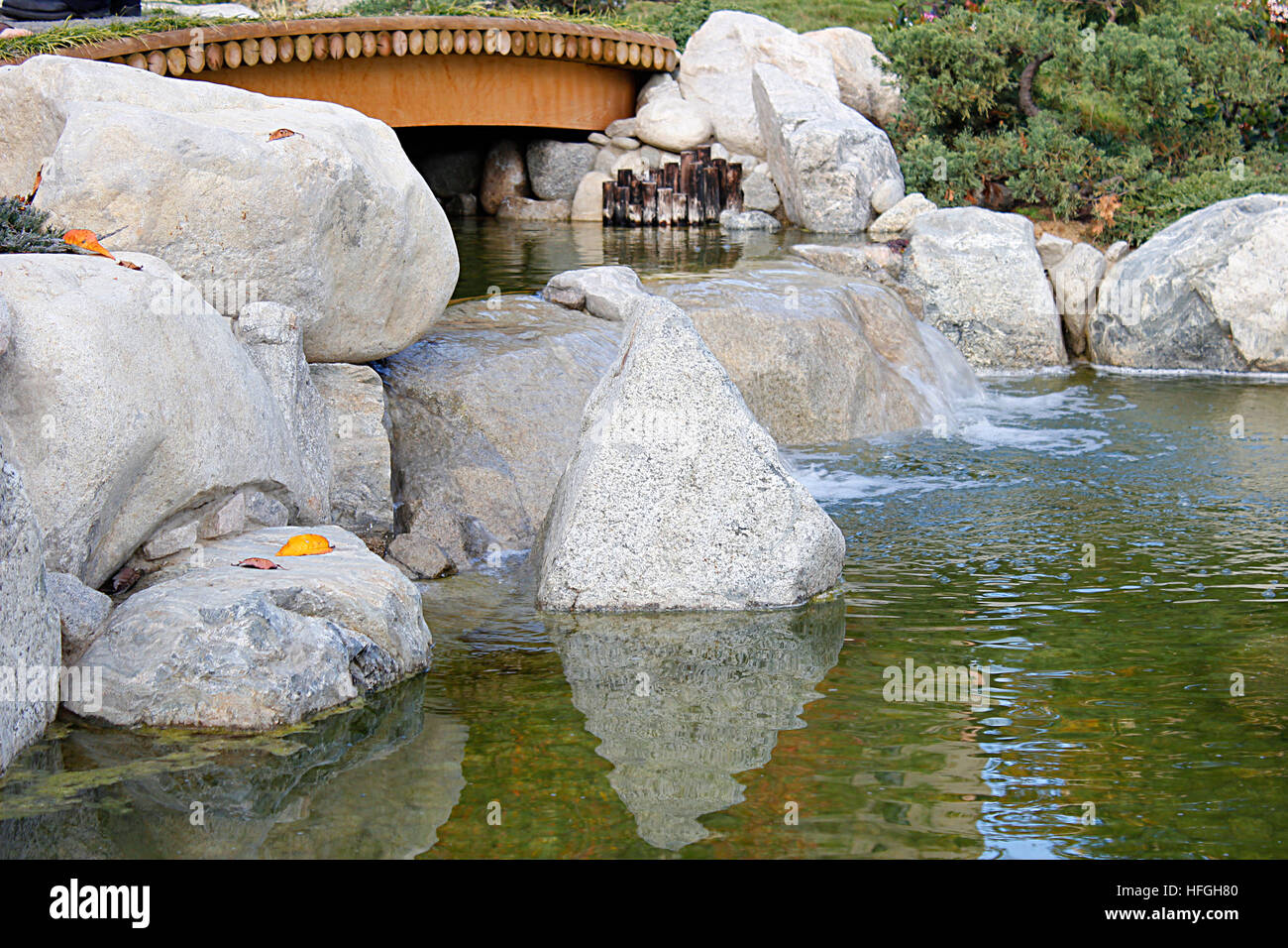 Waterfall through rocks into a pond with foliage around Stock Photo - Alamy