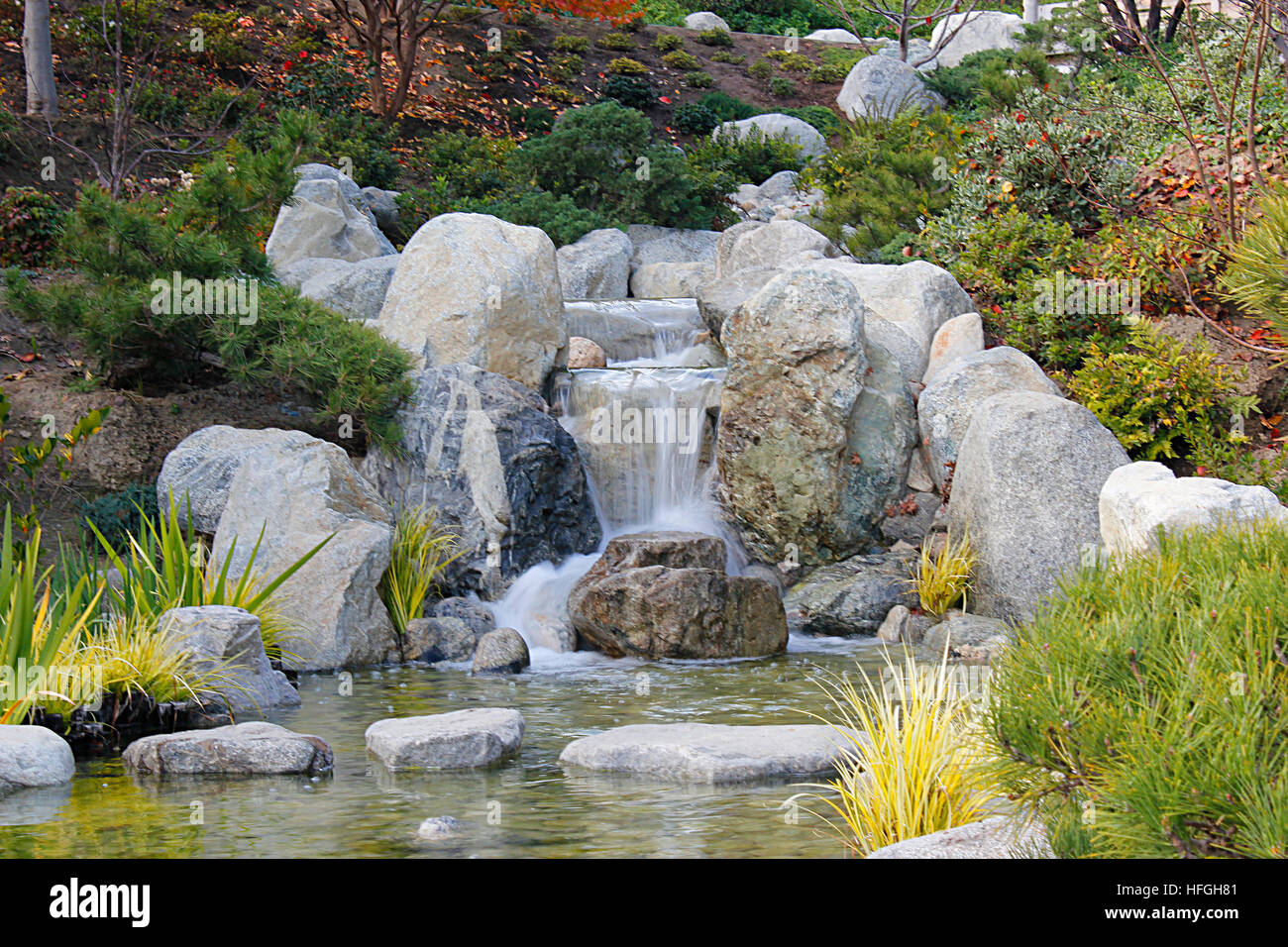 Waterfall through rocks into a pond with foliage around Stock Photo - Alamy