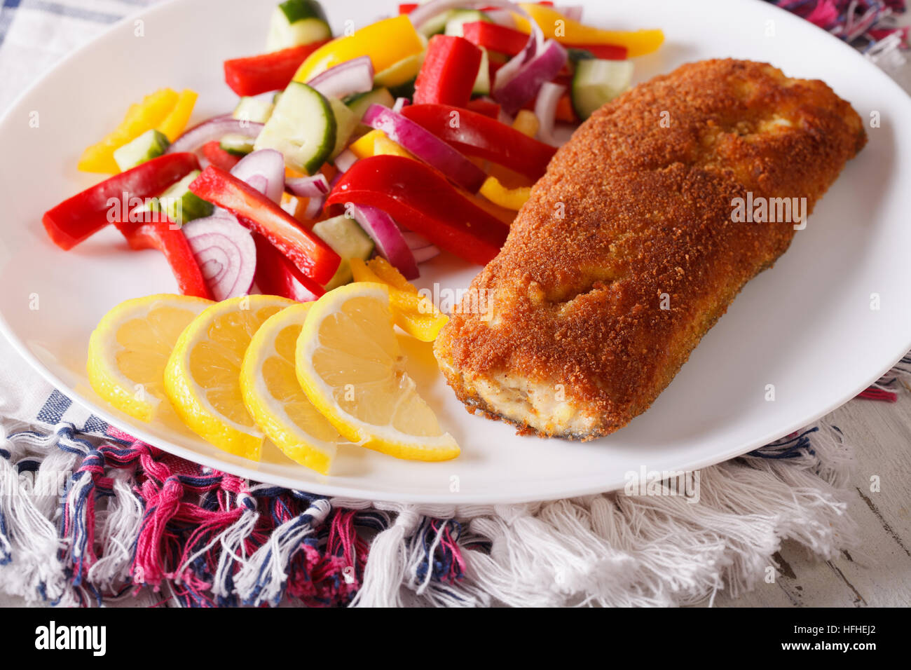 breaded fried fish with fresh salad and lemon on a plate close-up ...