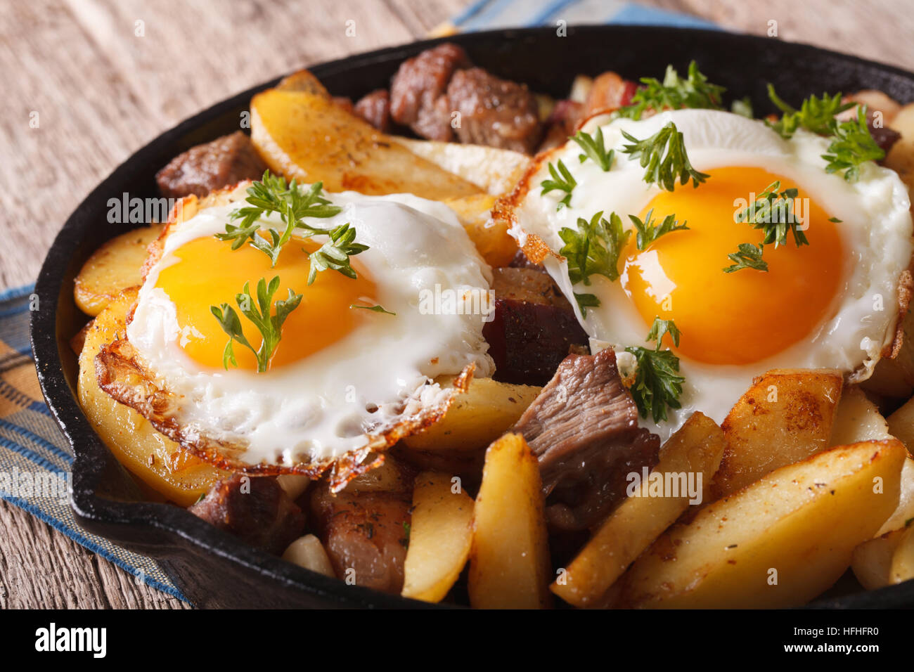Tyrolean food: fried potatoes with meat, ham and eggs in a pan close-up ...