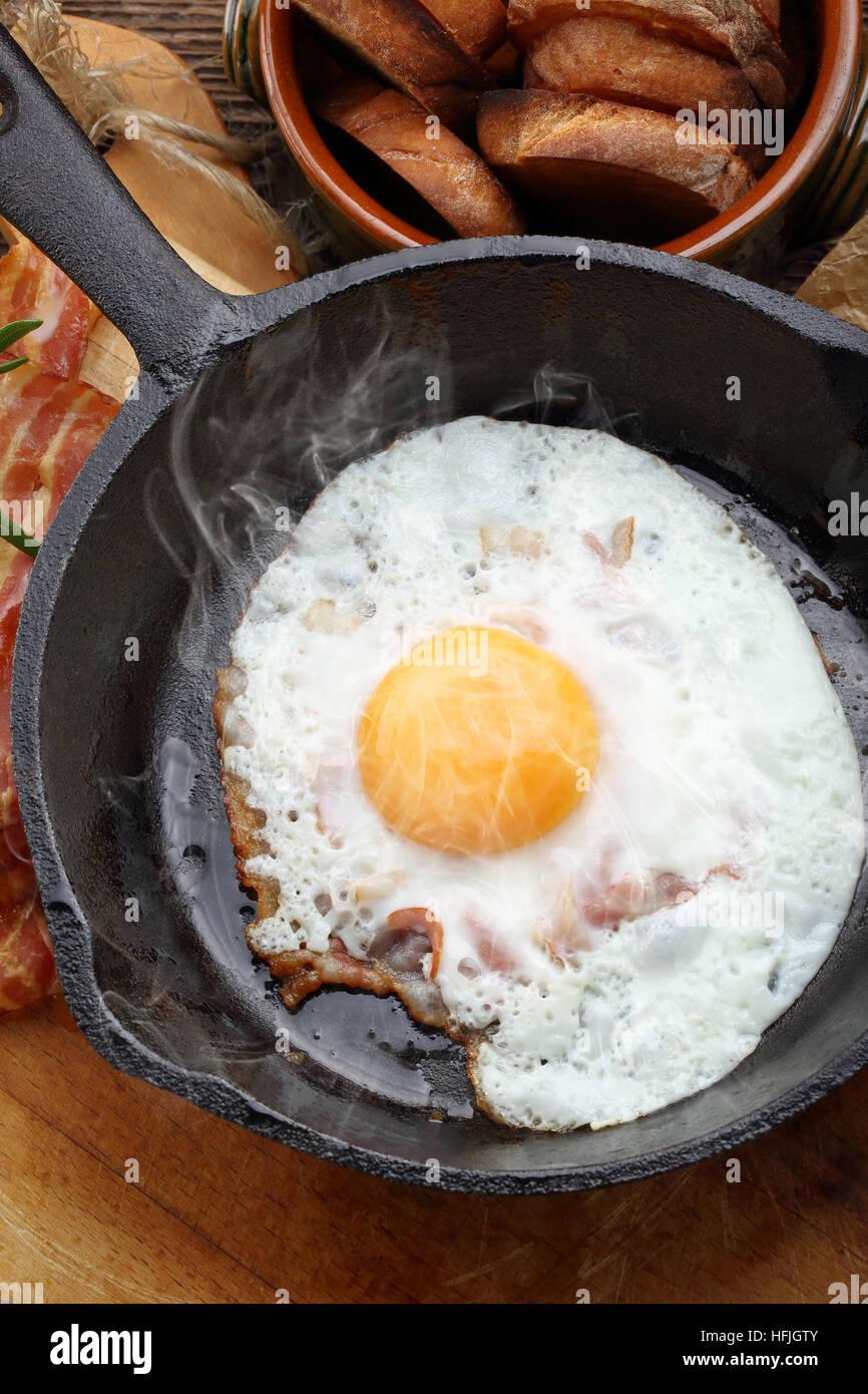 Fried hot egg with hot bacon pieces in a cast iron skillet Stock Photo ...