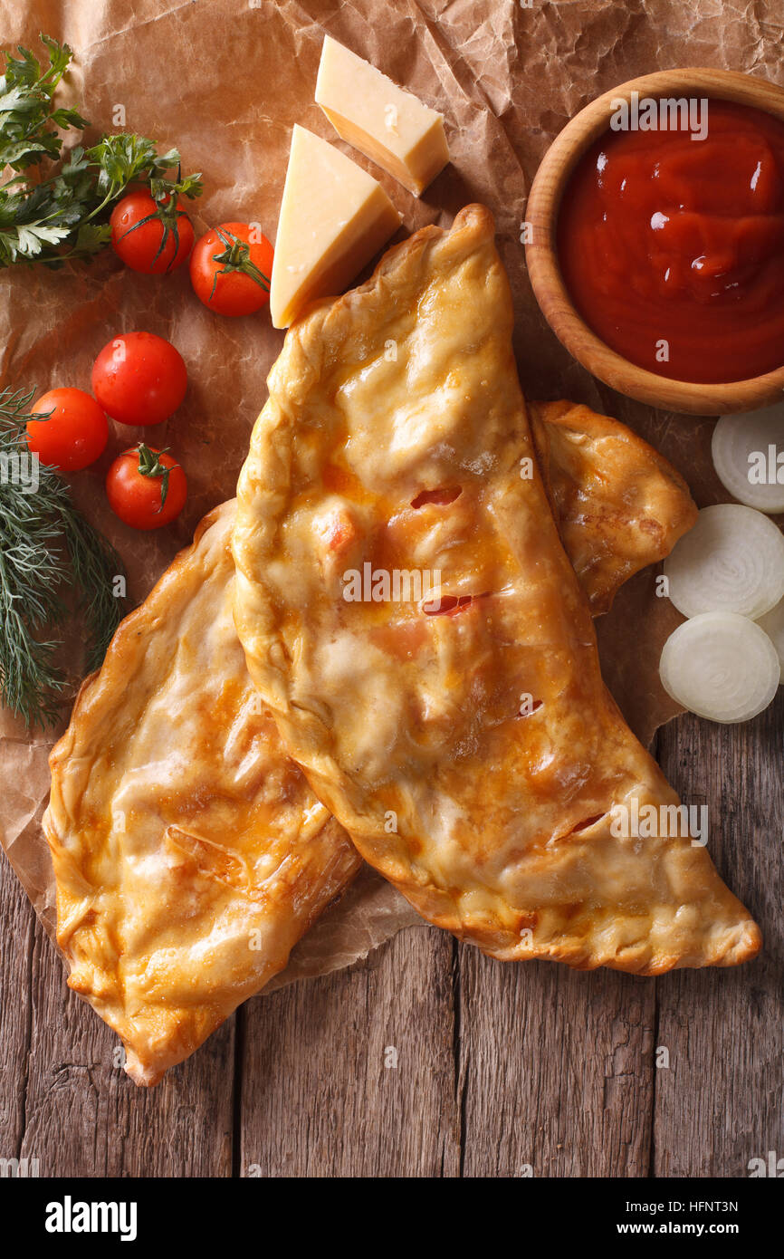 Italian pizza calzone closeup on a paper and ingredients. Vertical top ...