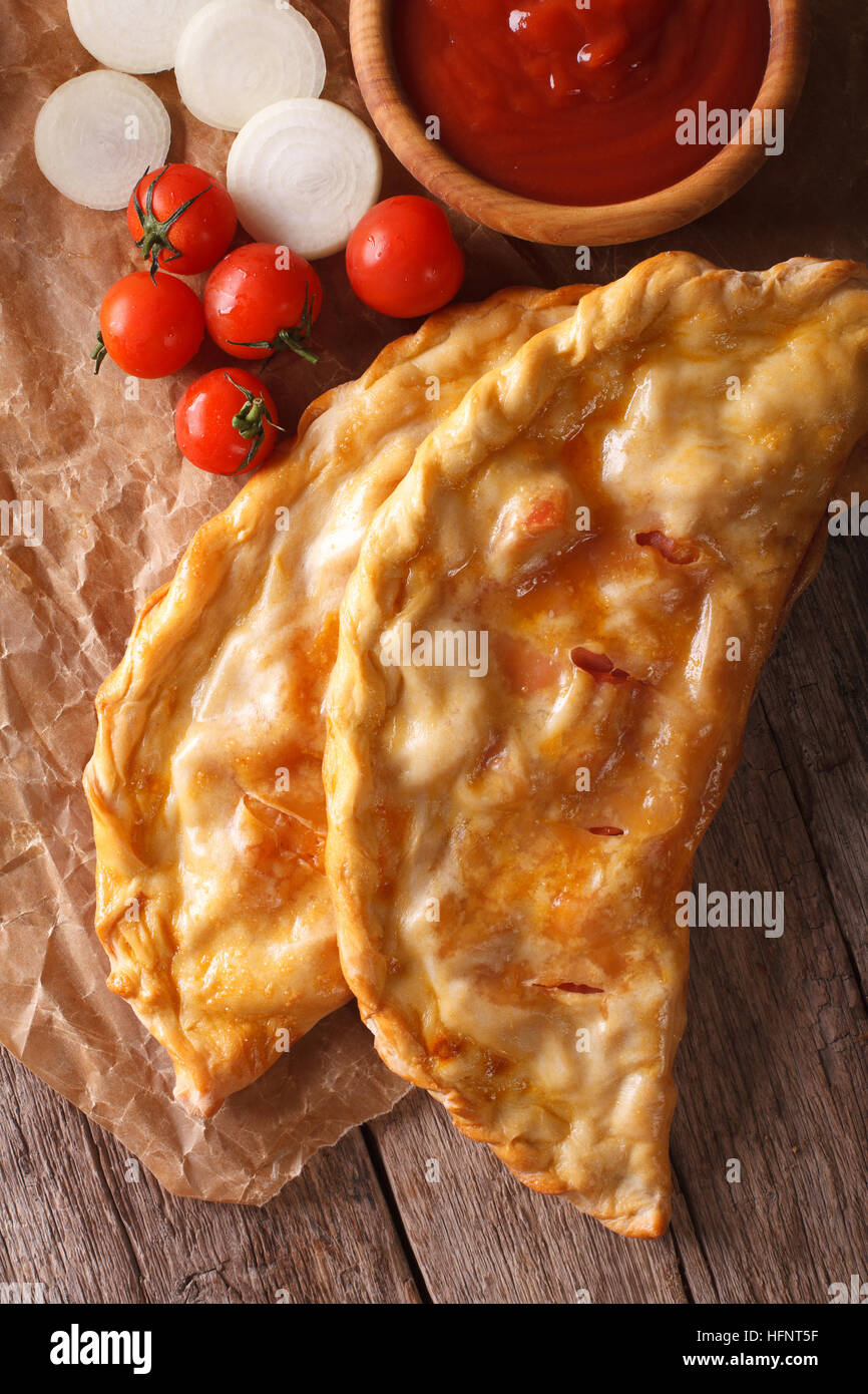 Italian pizza calzone closeup on a paper and ingredients. vertical top ...