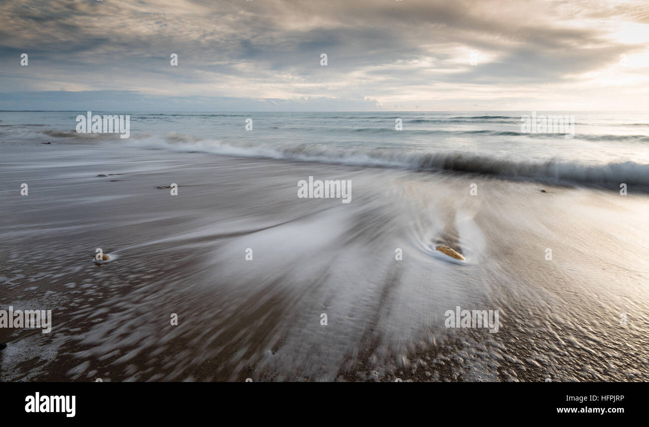 Pebbles on the beach on a black sand and flowing sea water creating ...