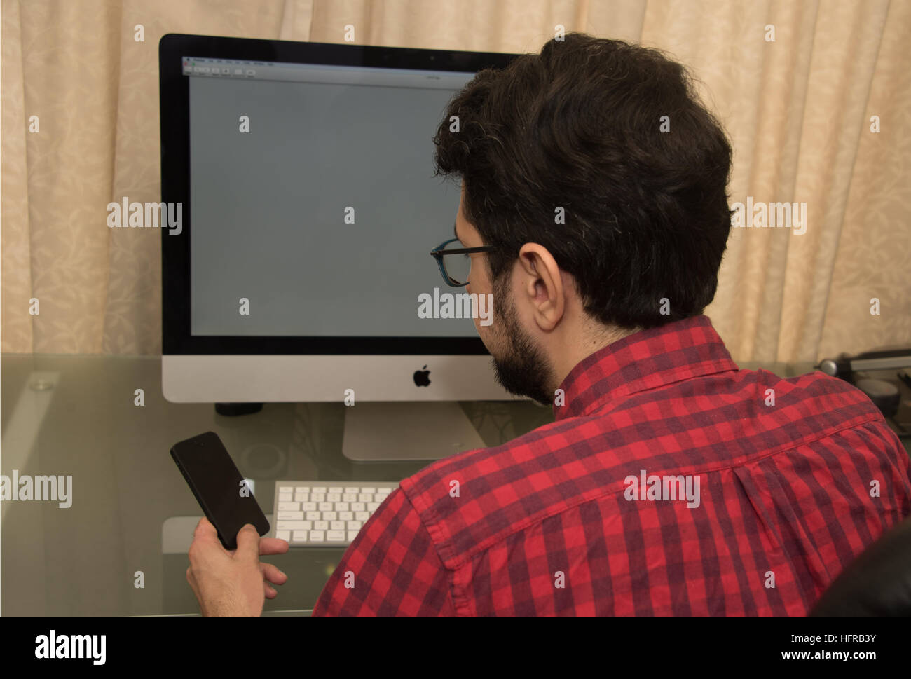 Young man sitting in front of a desktop computer with a smartphone ...