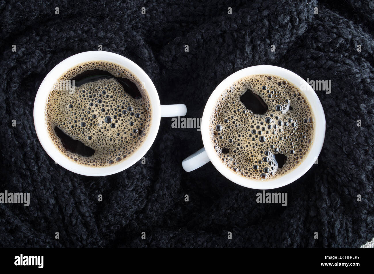 Top view of two small cups of coffee surrounded by a black woolen scarf ...