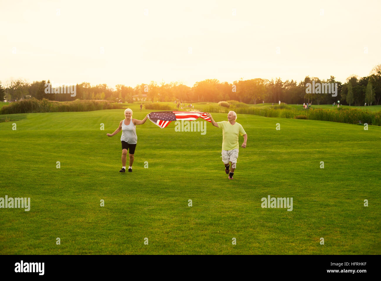 People running with American flag. Senior couple on nature background ...