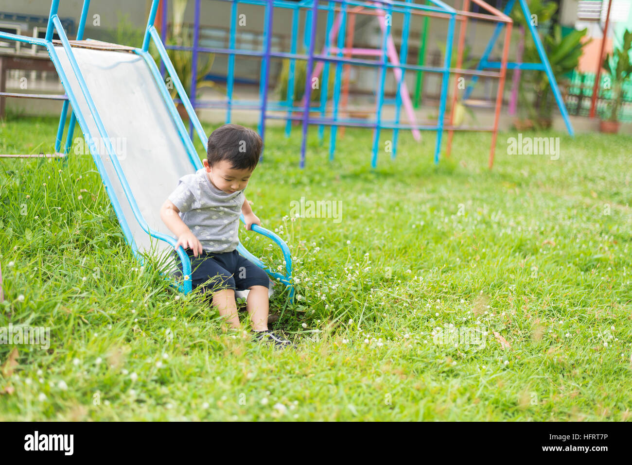 Little Asian kid playing slide at the playground under the sunlight in ...