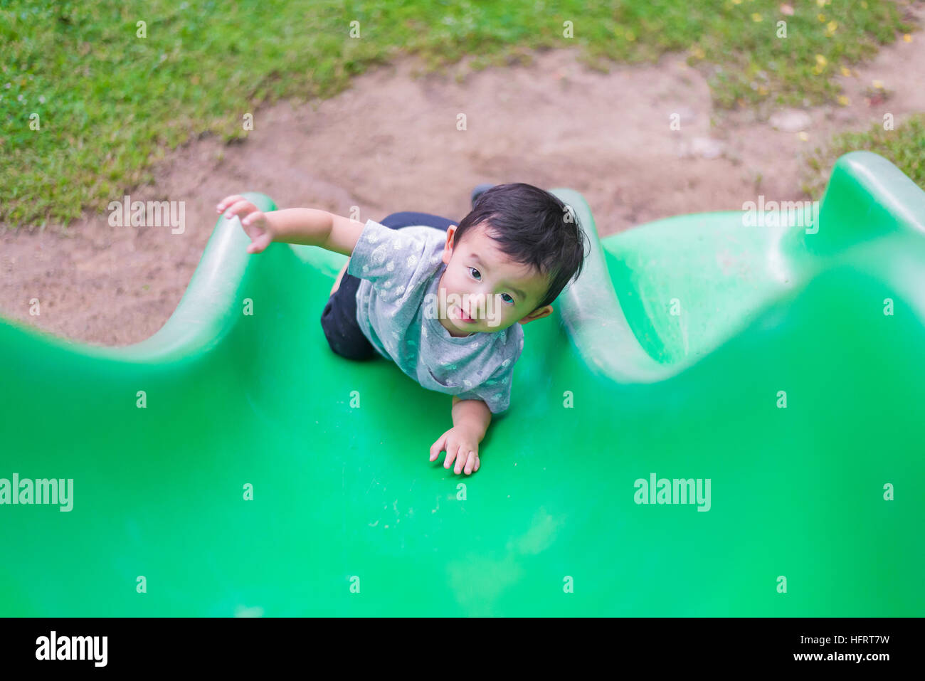 Little Asian kid climbing up the slide at the playground under the ...