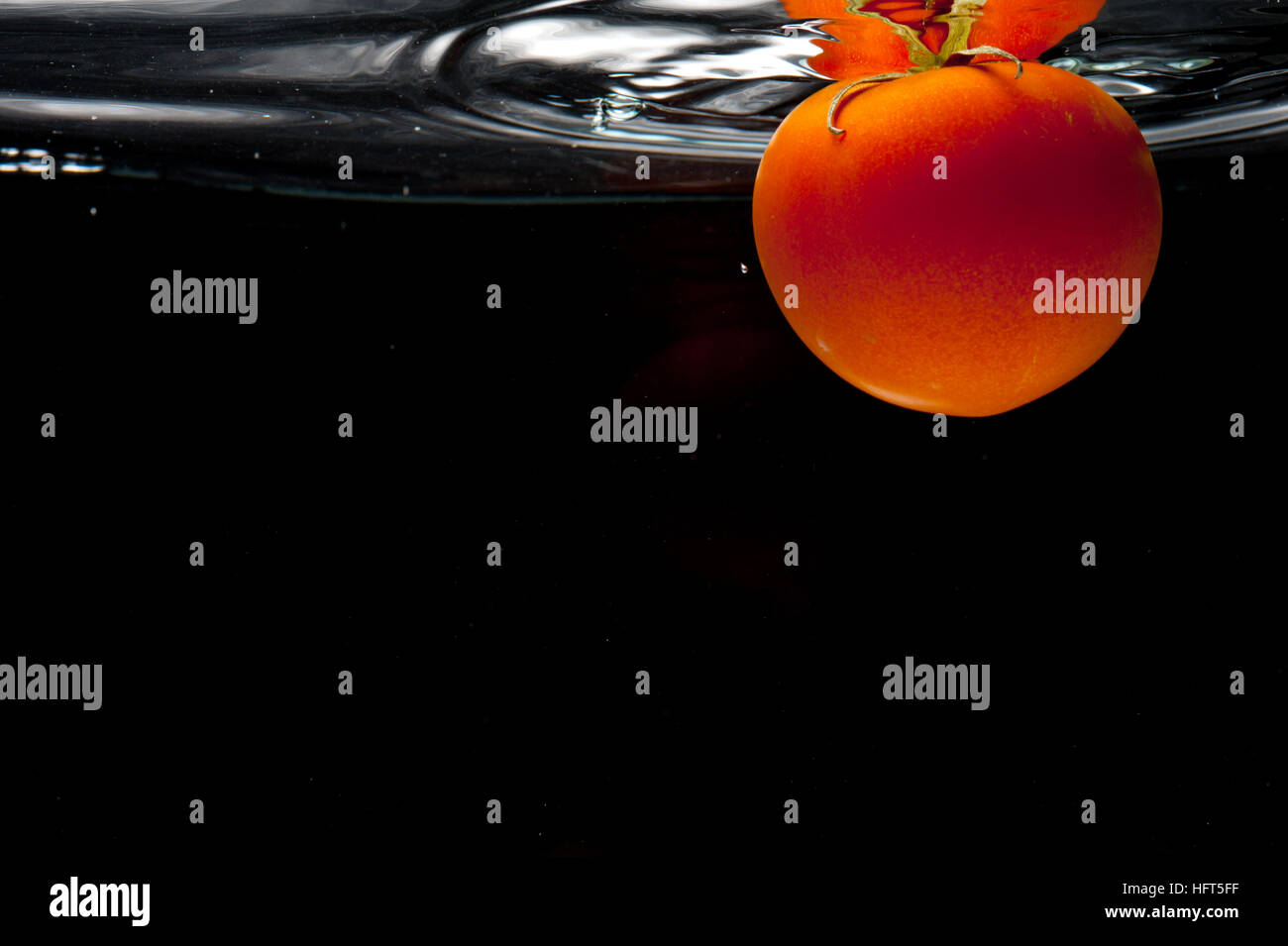 Tomato floating in the water on a black background Stock Photo - Alamy
