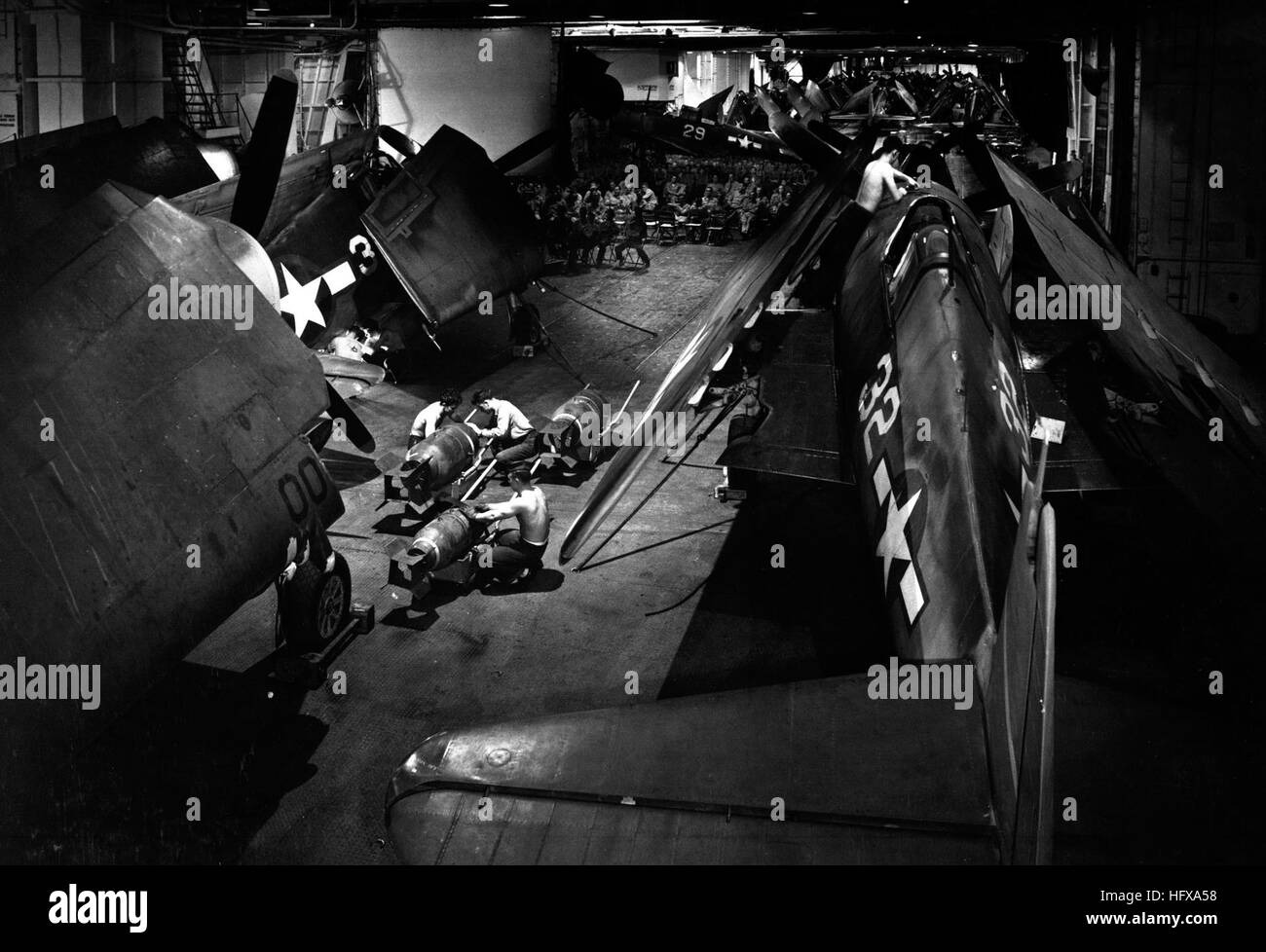 Surrounded by F6F's, ordnancemen work on bombs on hangar deck of USS ...
