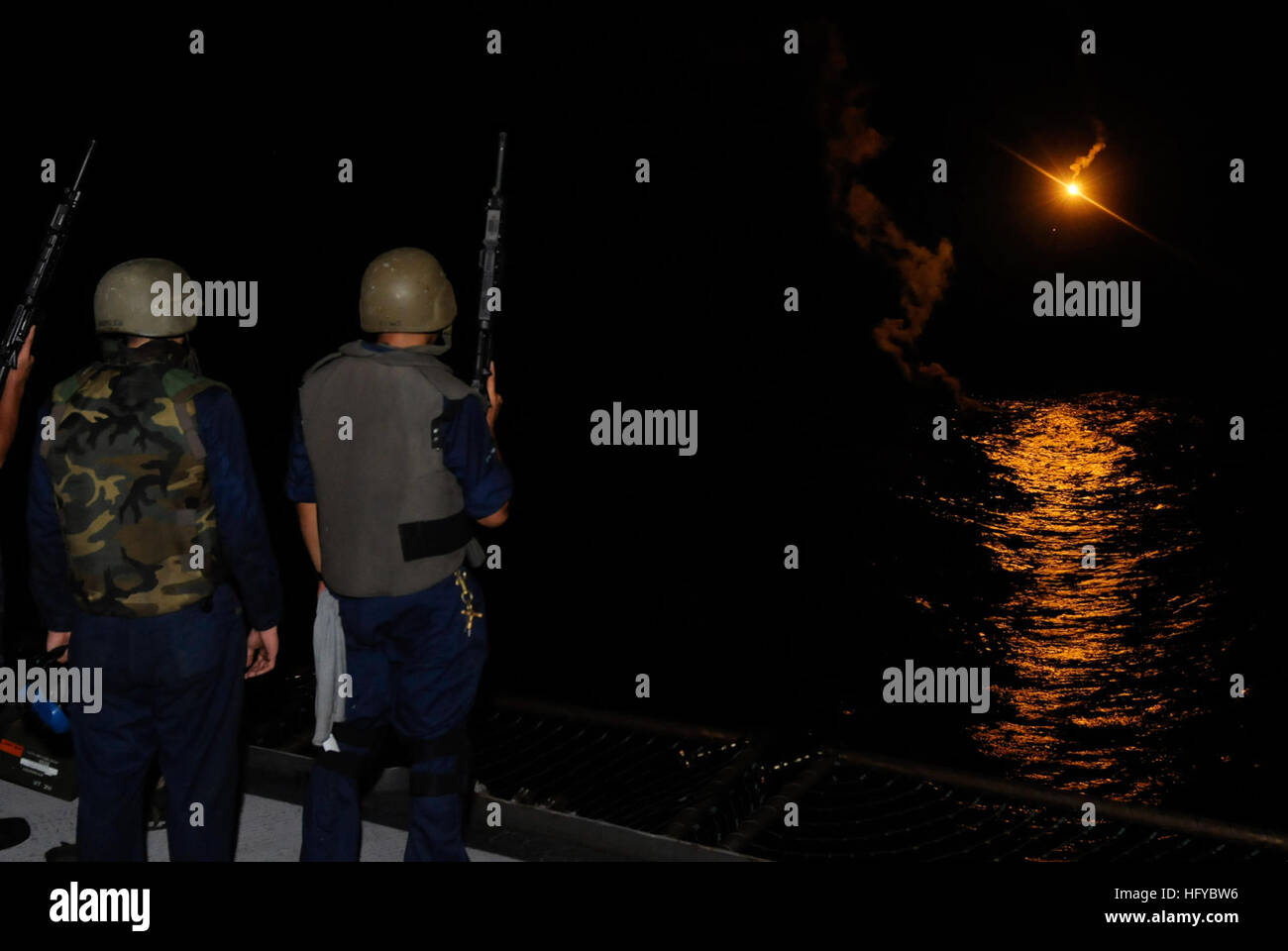 Sailors watch as a parachute flare descends into the ocean during 40mm ...