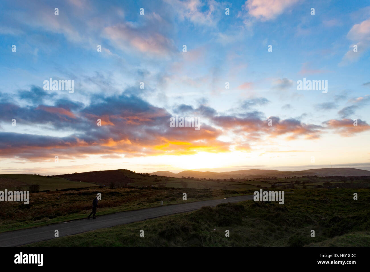 Sun setting over the Clwydian HIlls in the distance as a walker enjoys ...