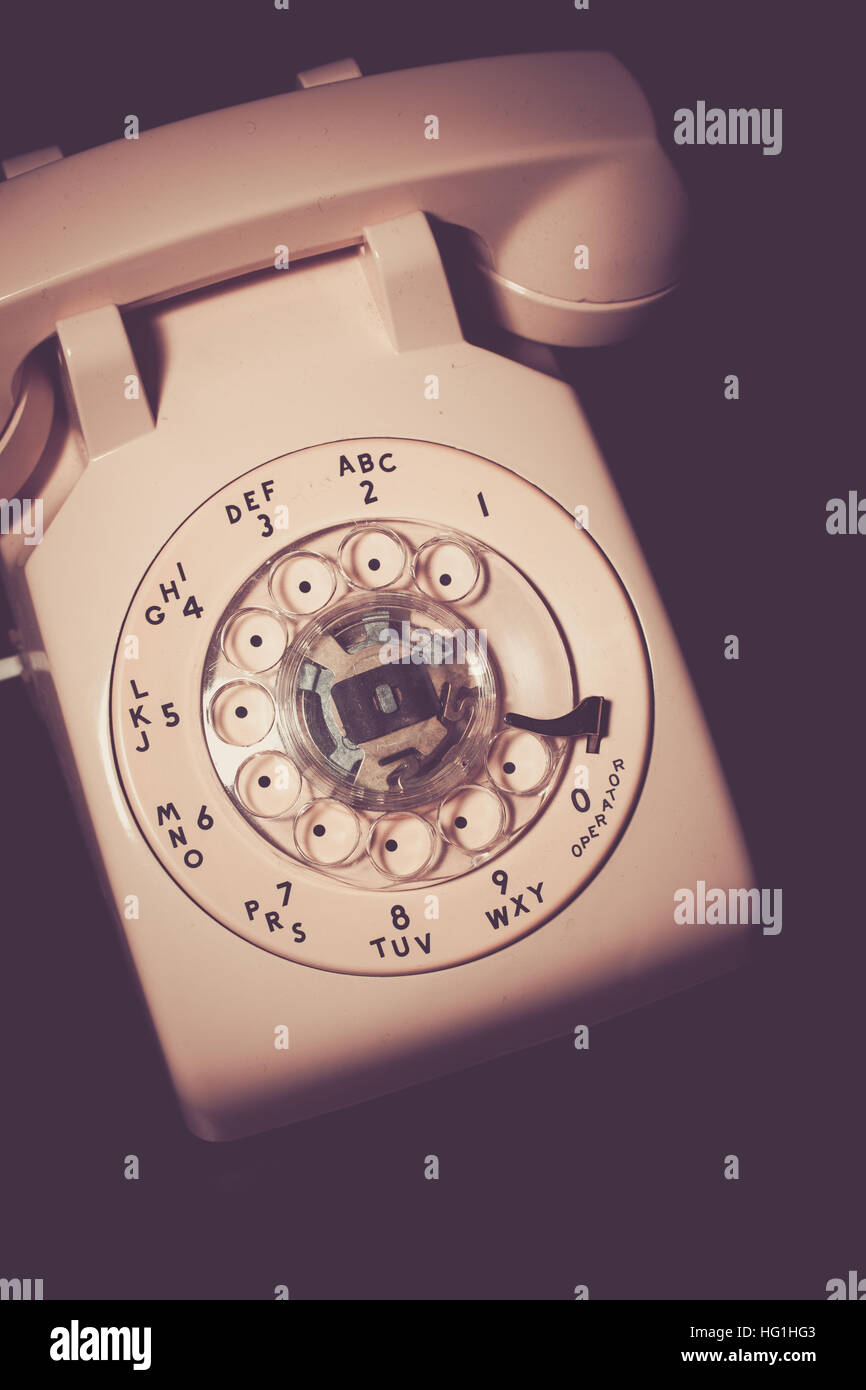 An old cream colored rotary phone sits on a black background Stock ...