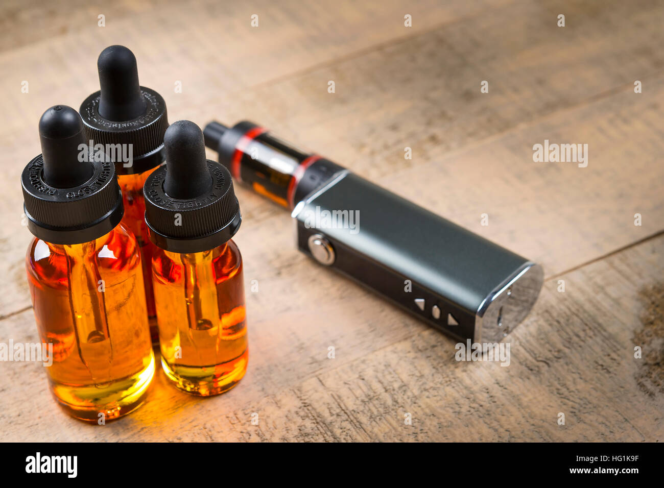 Vaping mod e-cig with tank atomizer and juice bottles over wood ...