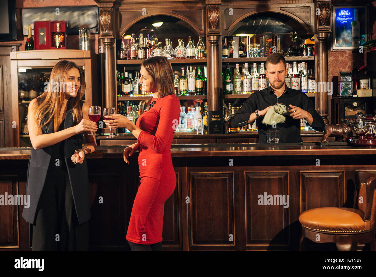Two attractive young women meeting up in a pub for a glass of red wine ...