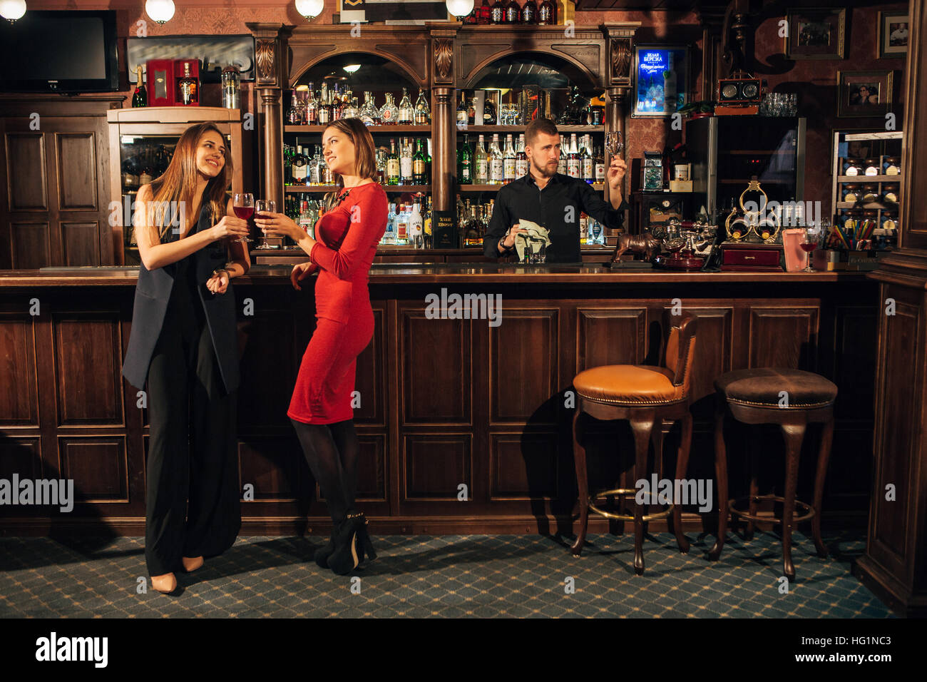 Two attractive young women meeting up in a pub for a glass of red wine ...