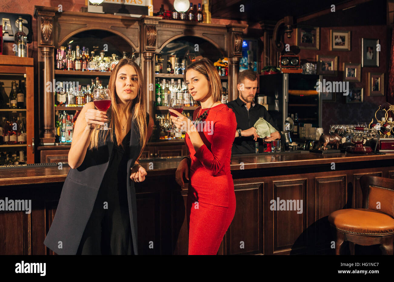 Two attractive young women meeting up in a pub for a glass of red wine ...