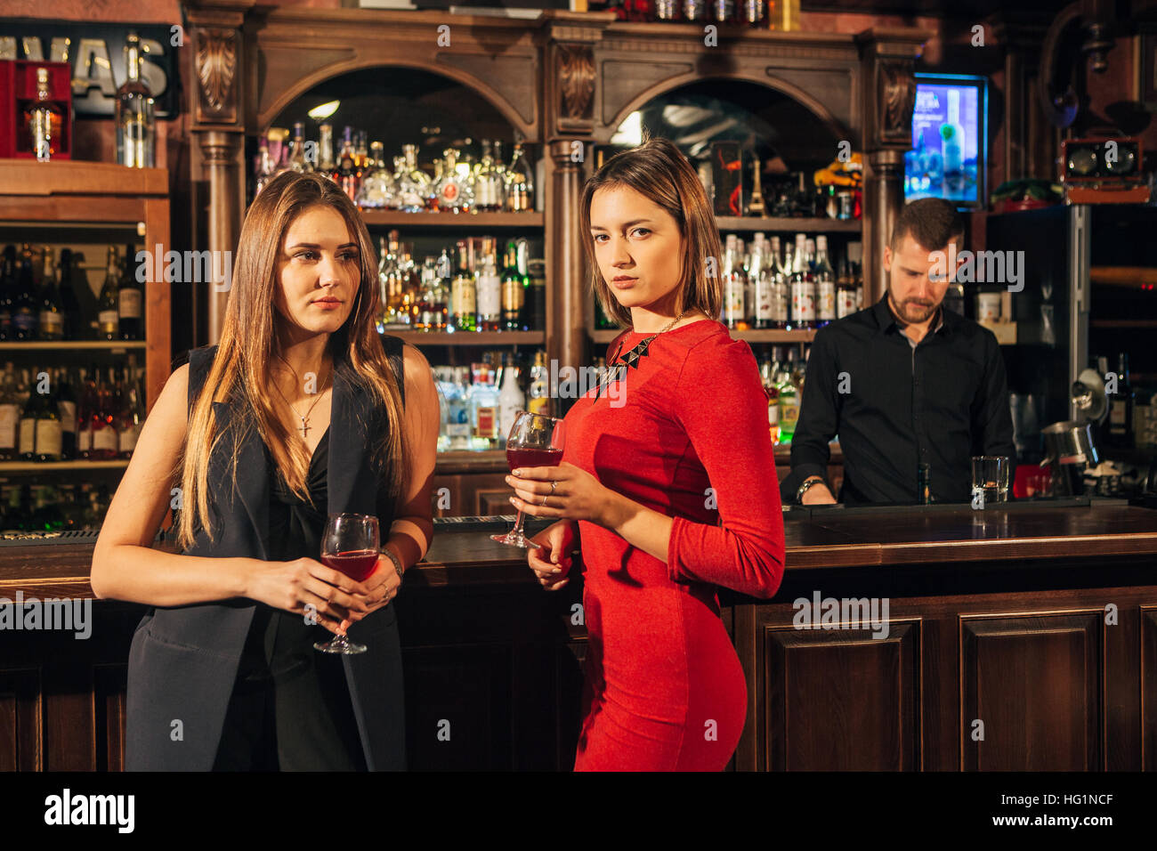 Two attractive young women meeting up in a pub for a glass of red wine ...