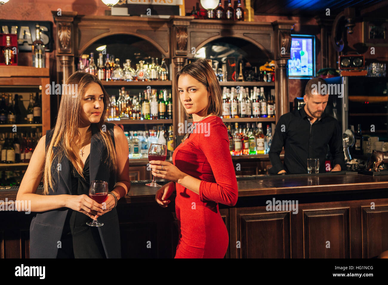 Two attractive young women meeting up in a pub for a glass of red wine ...