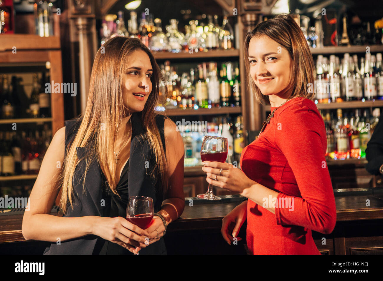 Two attractive young women meeting up in a pub for a glass of red wine ...