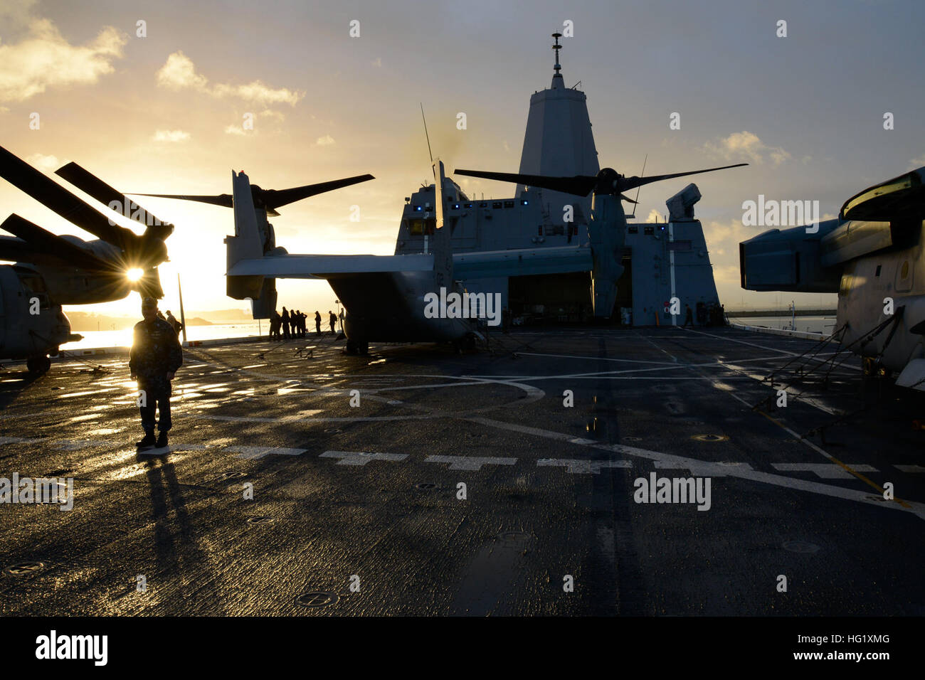 U.S. Sailors watch the sun rise on the flight deck of the amphibious ...