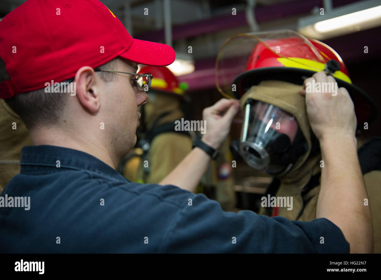 Damage Controlman 2nd Class Garrett Calebaugh helps a Sailor don a ...