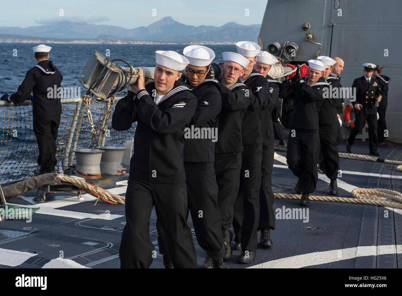 Sailors carry a flag staff across the flight deck of Arleigh Burke ...