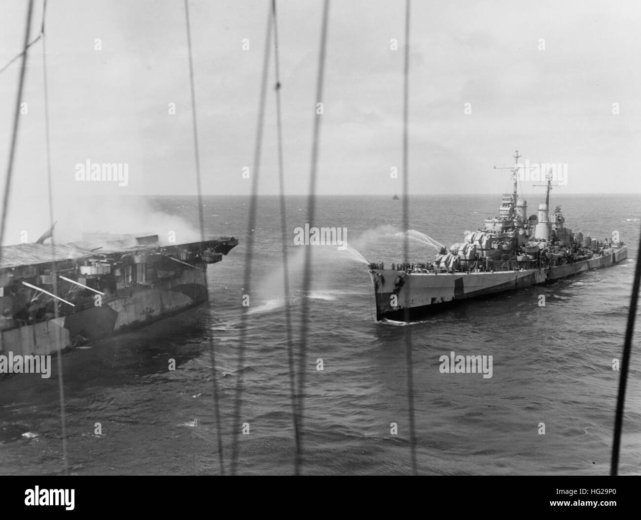 USS Reno (CL-96) comes alongside the burning USS Princeton (CVL-23) to ...