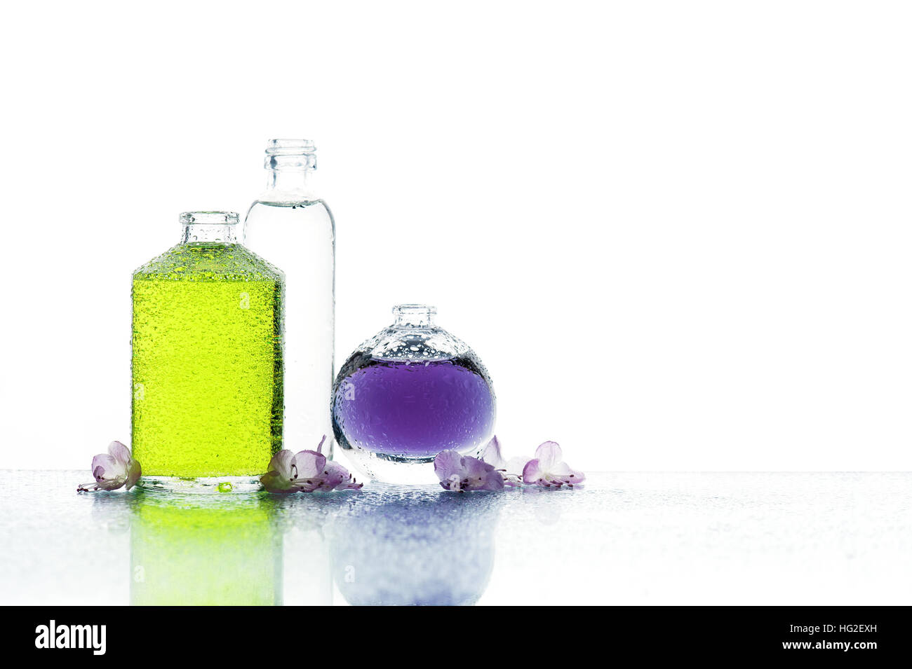 Three various bottles with color liquid and flowers on the wet mirror ...