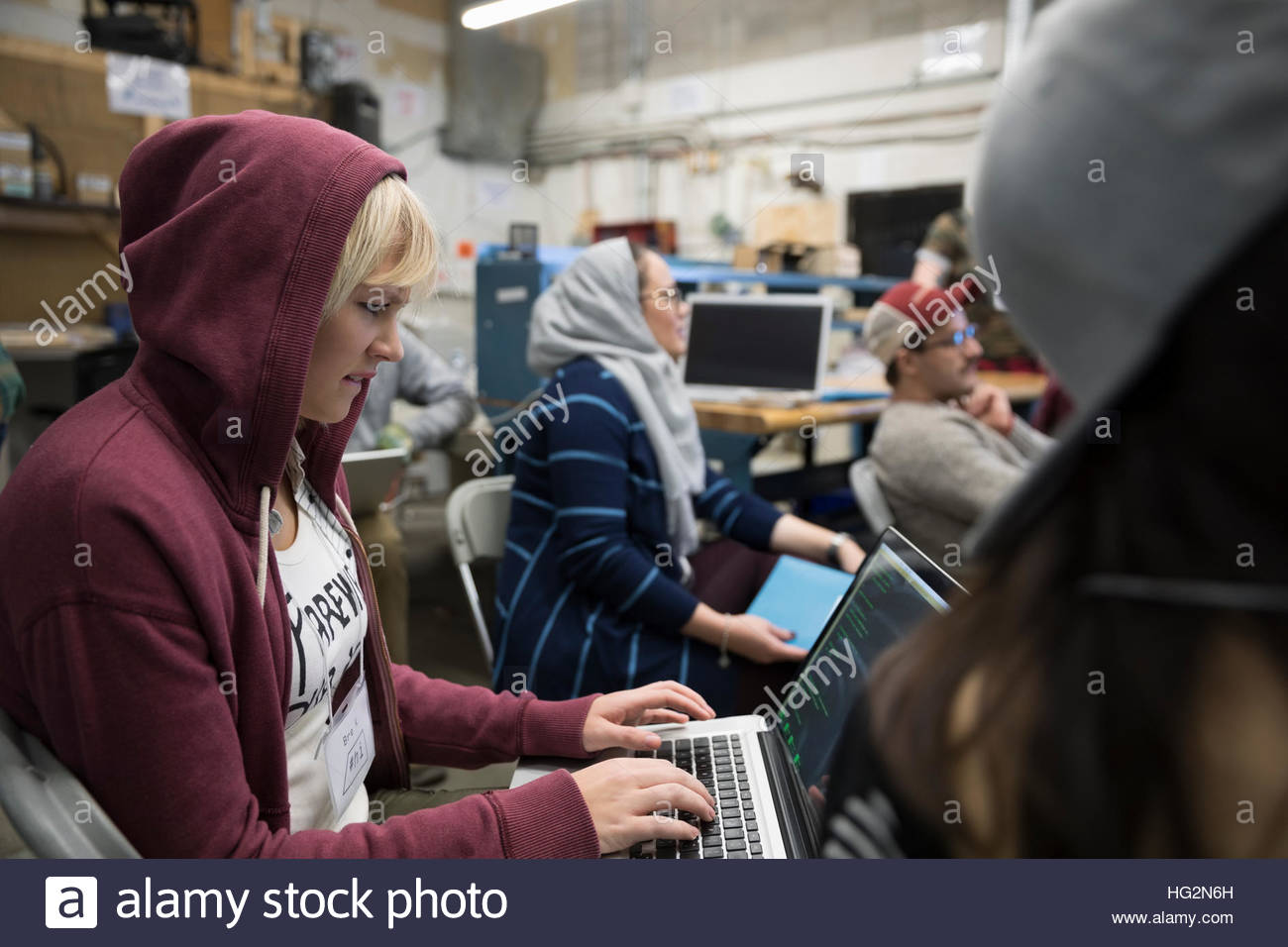 Female hacker wearing hoody working hackathon at laptop in workshop ...