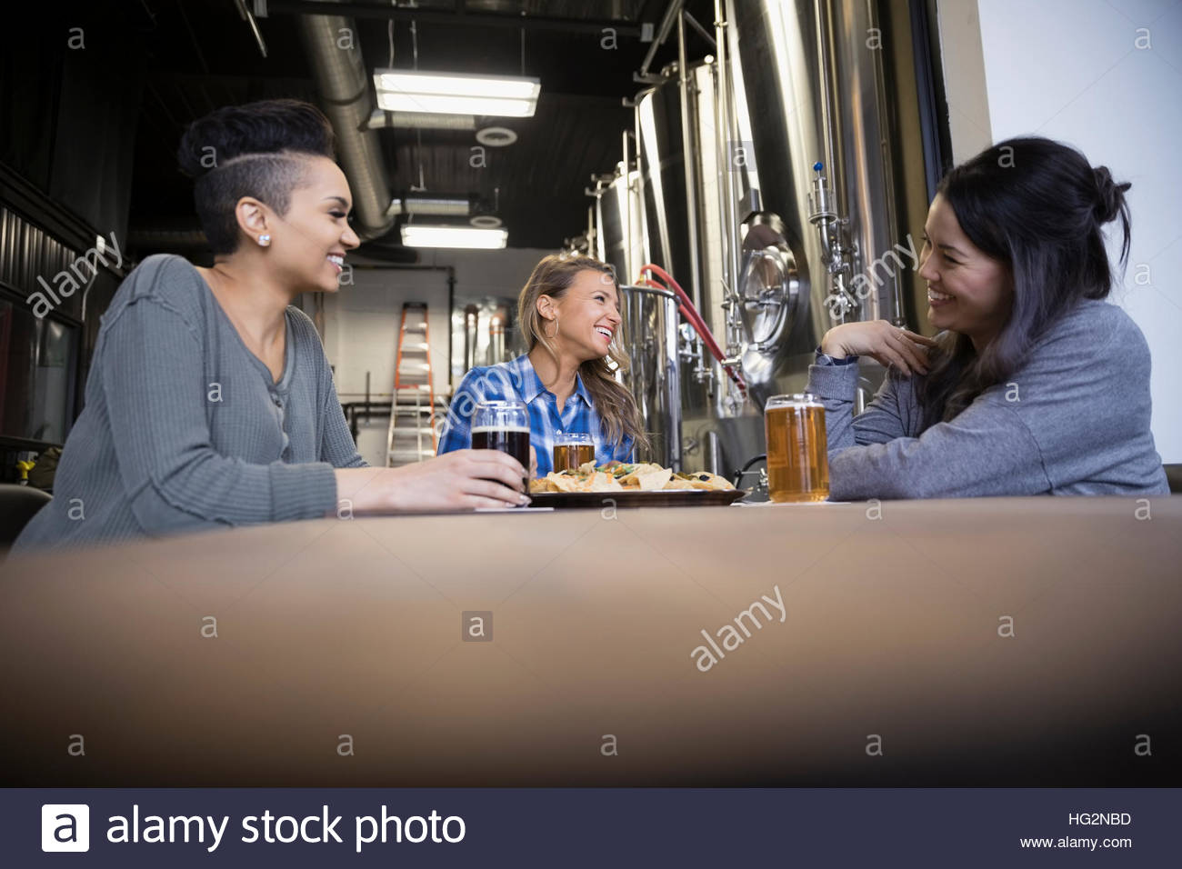 Smiling female friends drinking beers at brewery tasting room ...