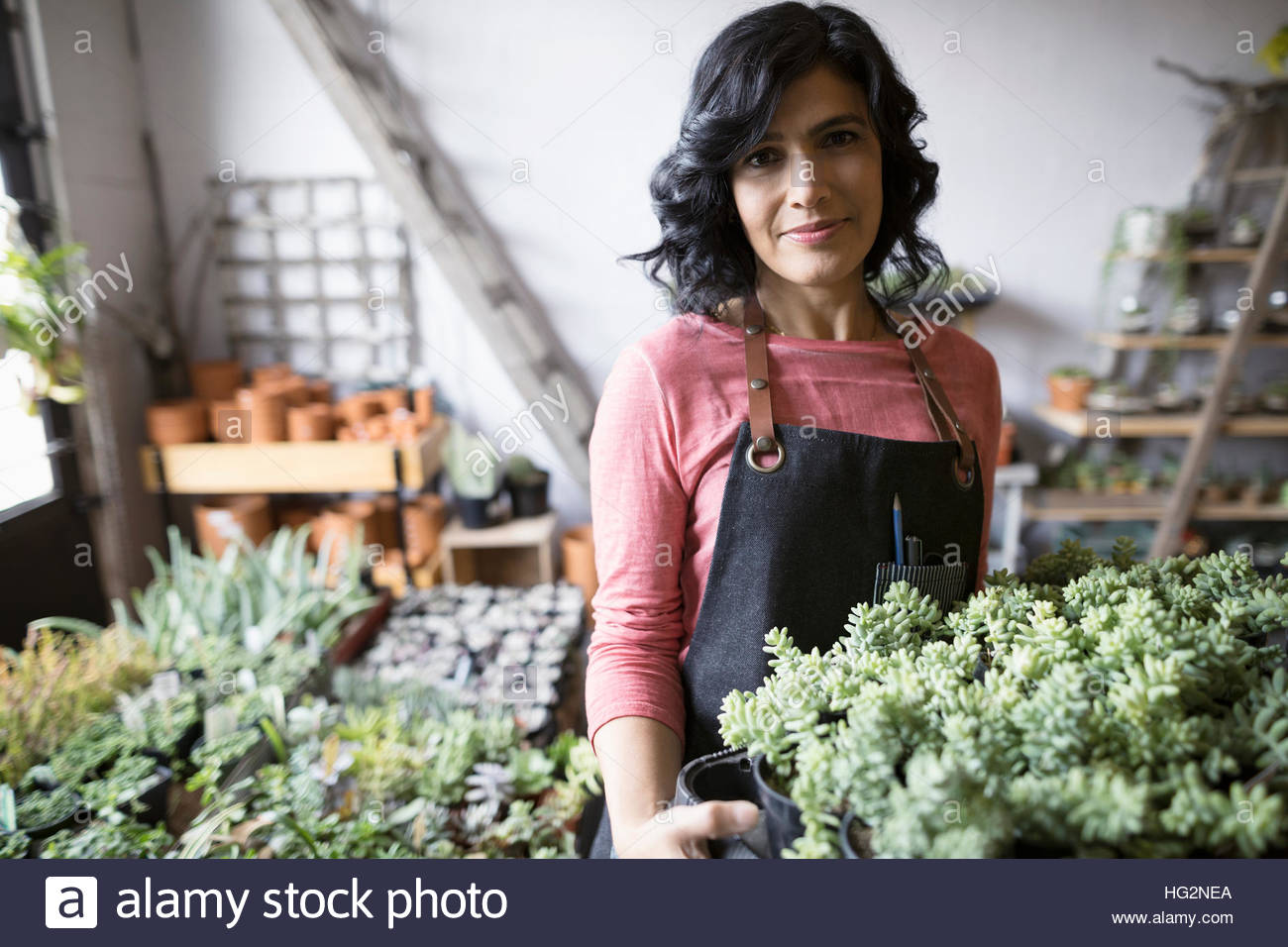 Portrait female shop owner holding tray of potted plants in plant shop ...