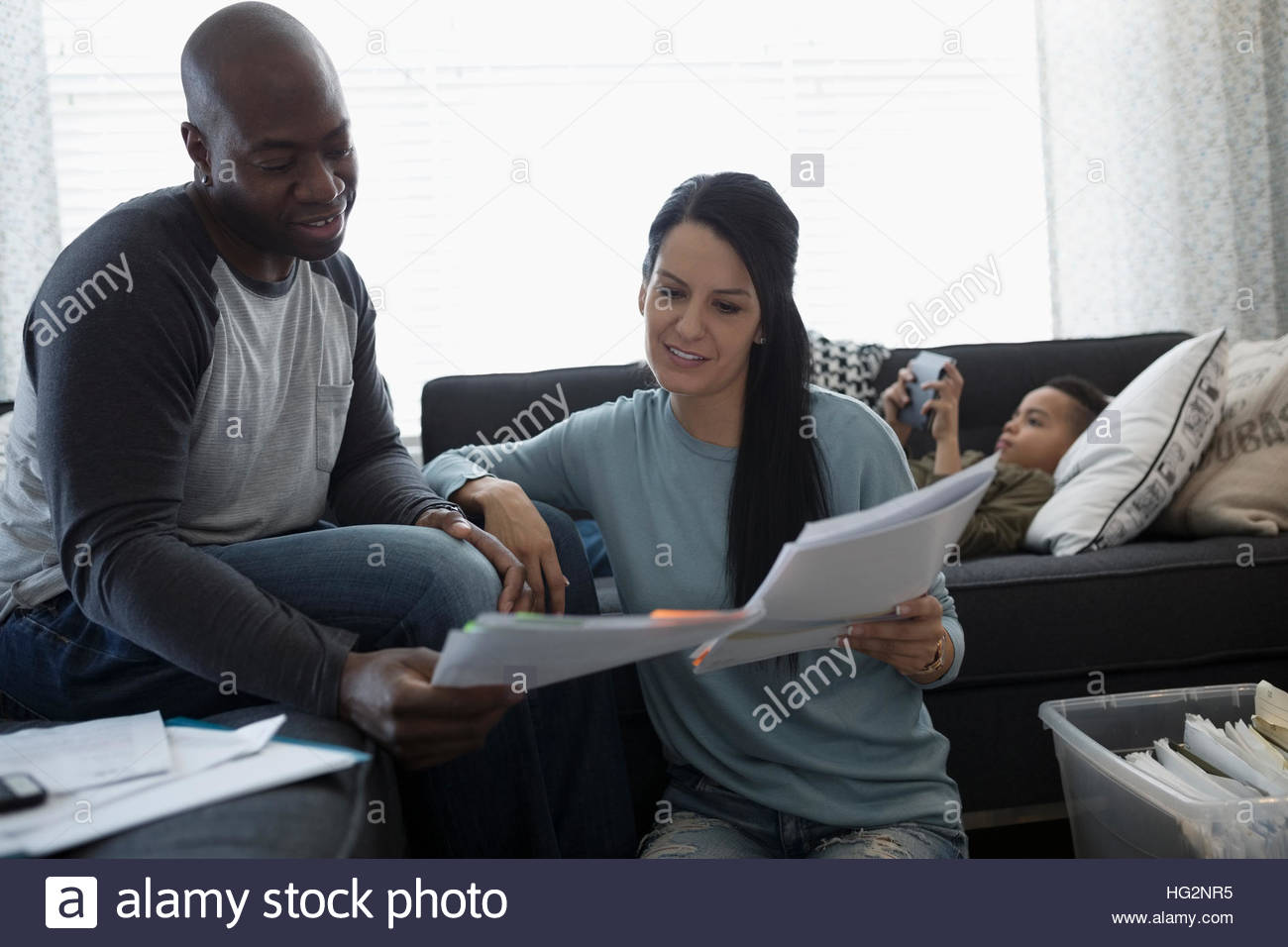 Couple reviewing financial paperwork on living room sofa with son in ...