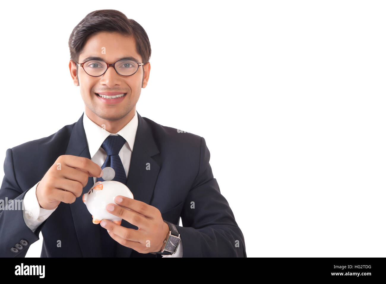 Happy looking young professional man dropping coin in small piggy bank ...