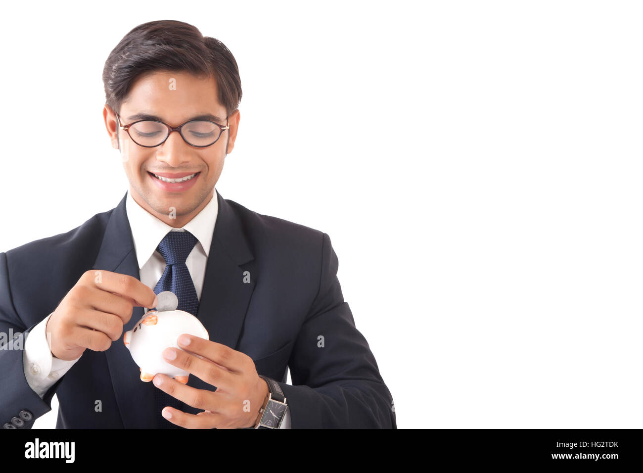 Happy looking young professional man dropping coin in small piggy bank ...