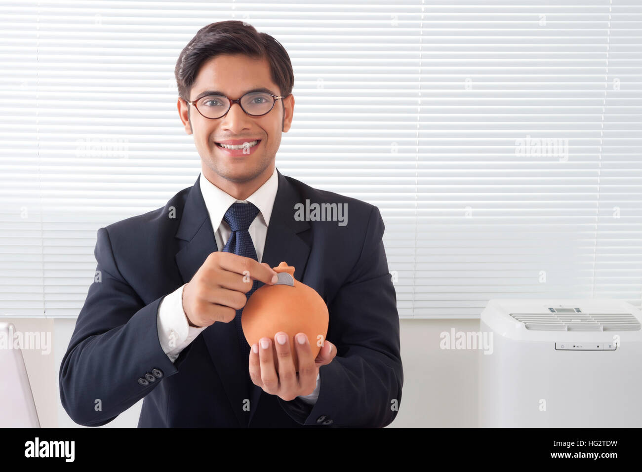 Happy looking young professional man dropping coin in clay saving pot ...