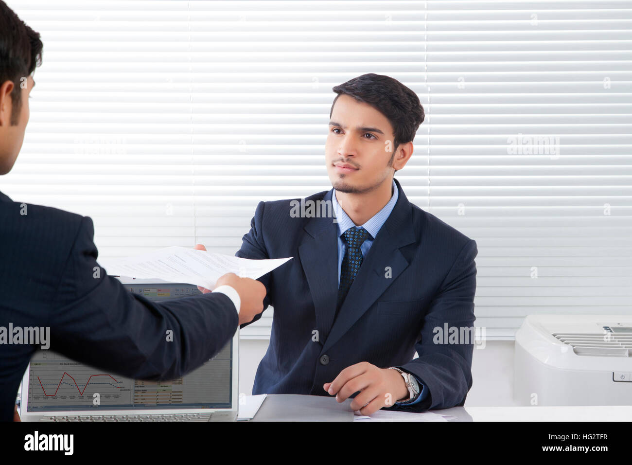 Businessman handing over document to young professional man in office ...