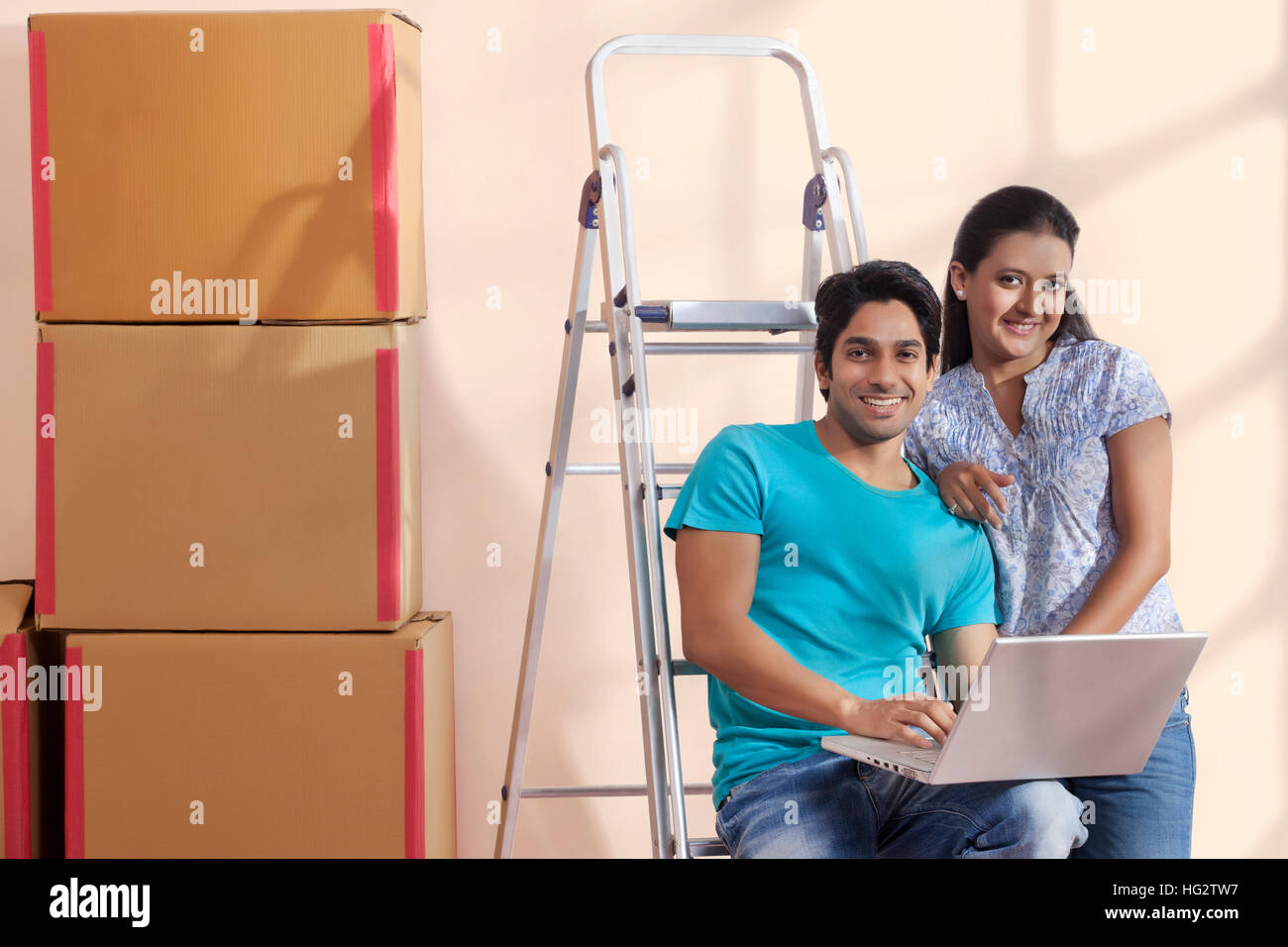 Portrait of a young couple using a laptop standing on ladder Stock ...