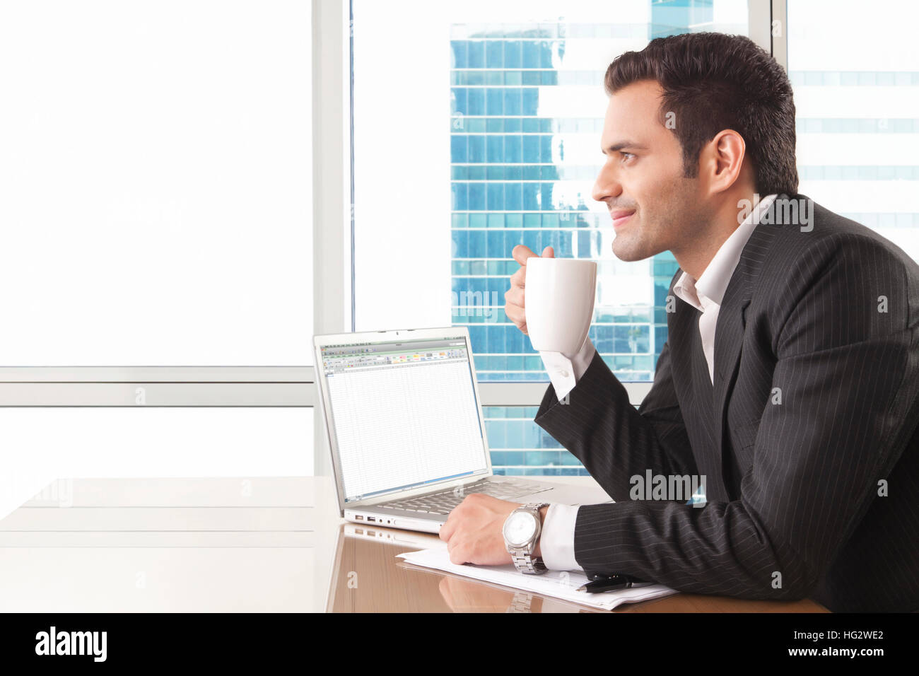 Smiling business man sitting at office desk and holding cup of tea in ...