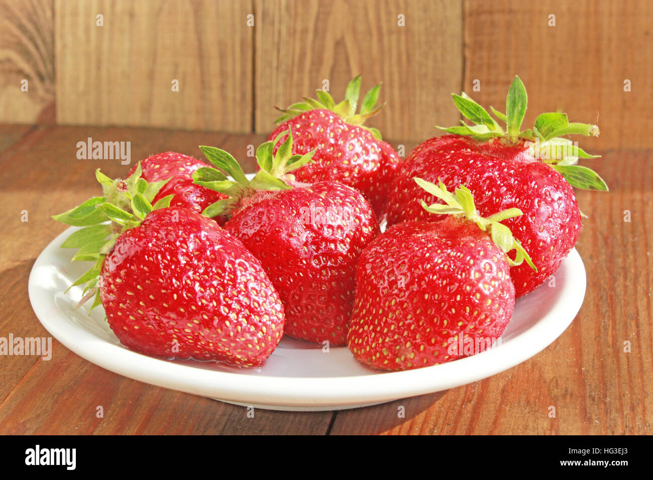 ripe red strawberries on the white plate on the brown background. Red ...
