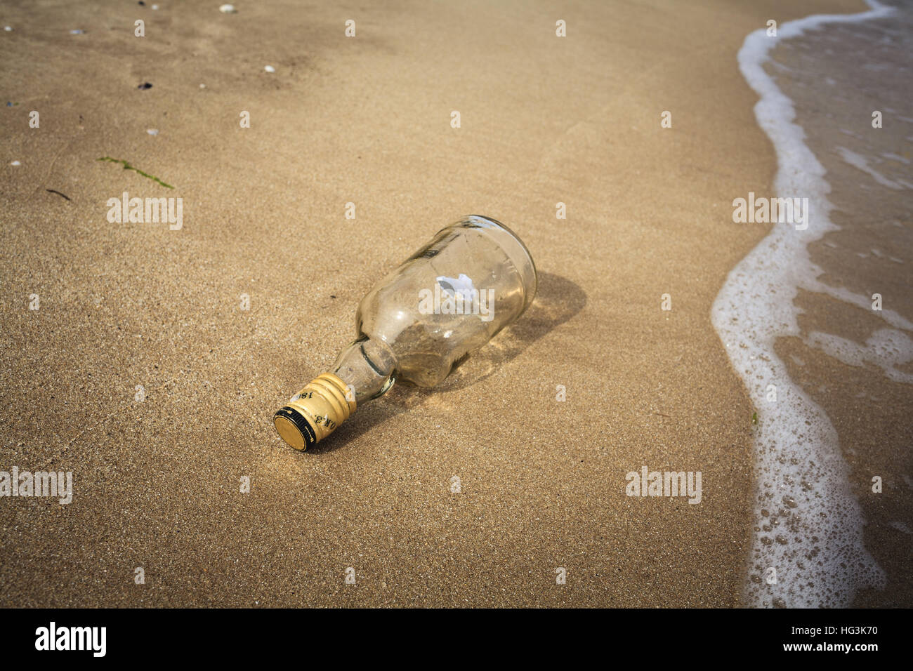 Empty bottle washed up at the sandy beach Stock Photo - Alamy