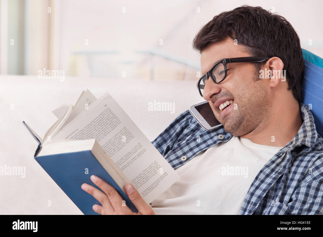 Smiling young man talking on phone while reading book Stock Photo - Alamy