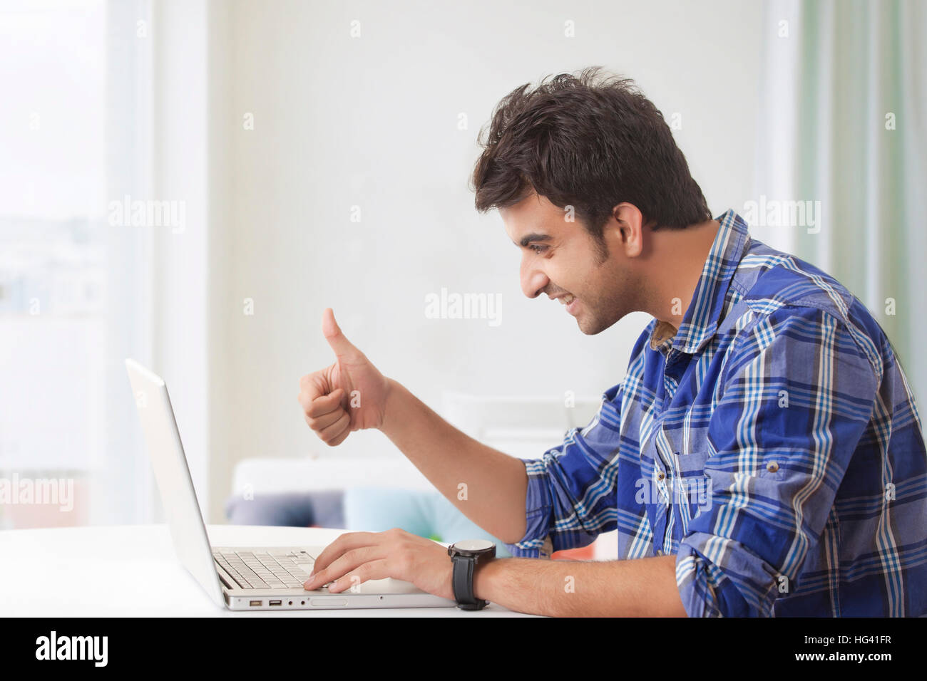Smiling man showing thumbs up while using laptop computer Stock Photo ...