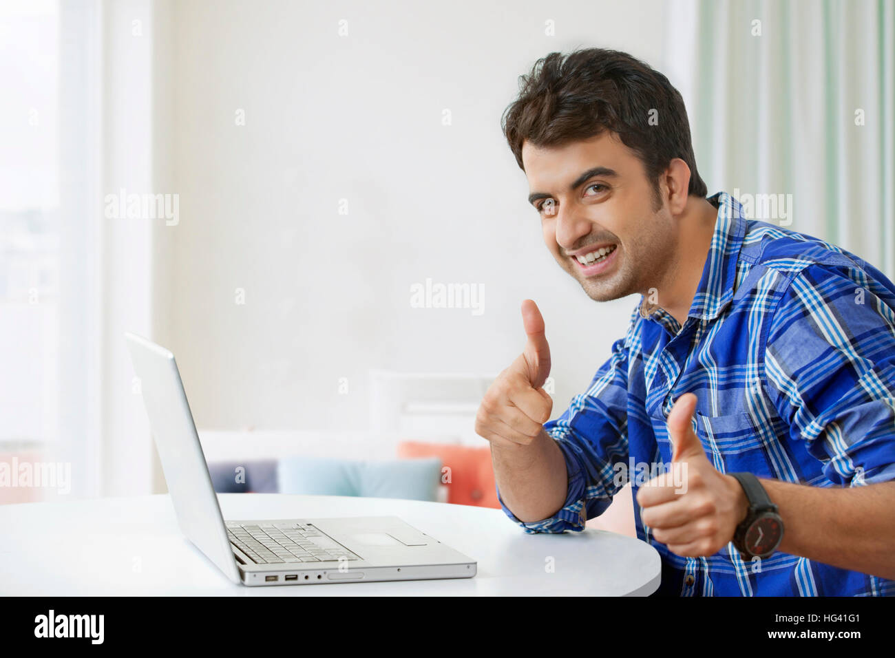 Smiling man showing thumbs up while using laptop computer Stock Photo ...